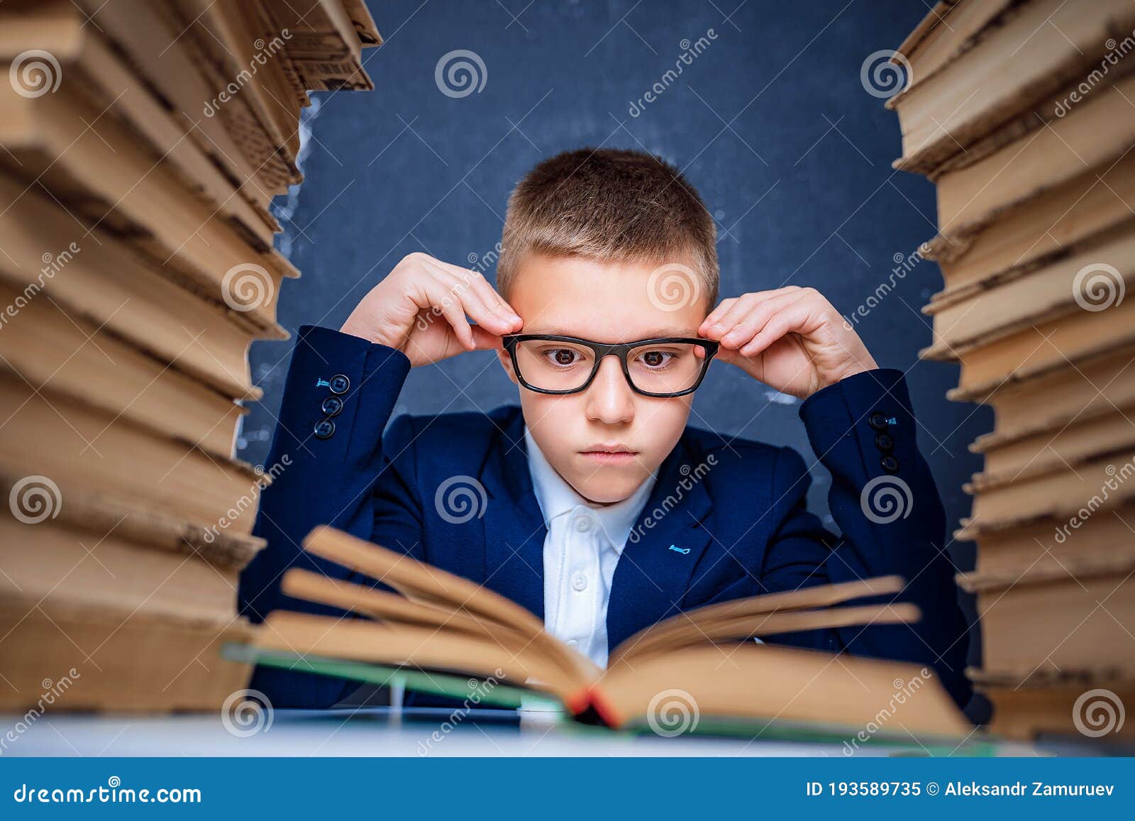 Smart Boy in Glasses Sitting between Two Piles of Books and Read Book ...