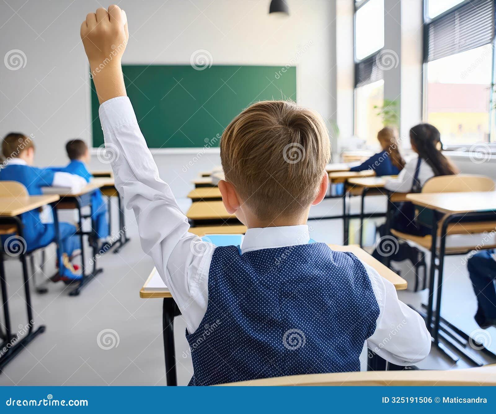 Smart Schoolboy Sits at a Desk in a Classroom with His Hand Raised ...