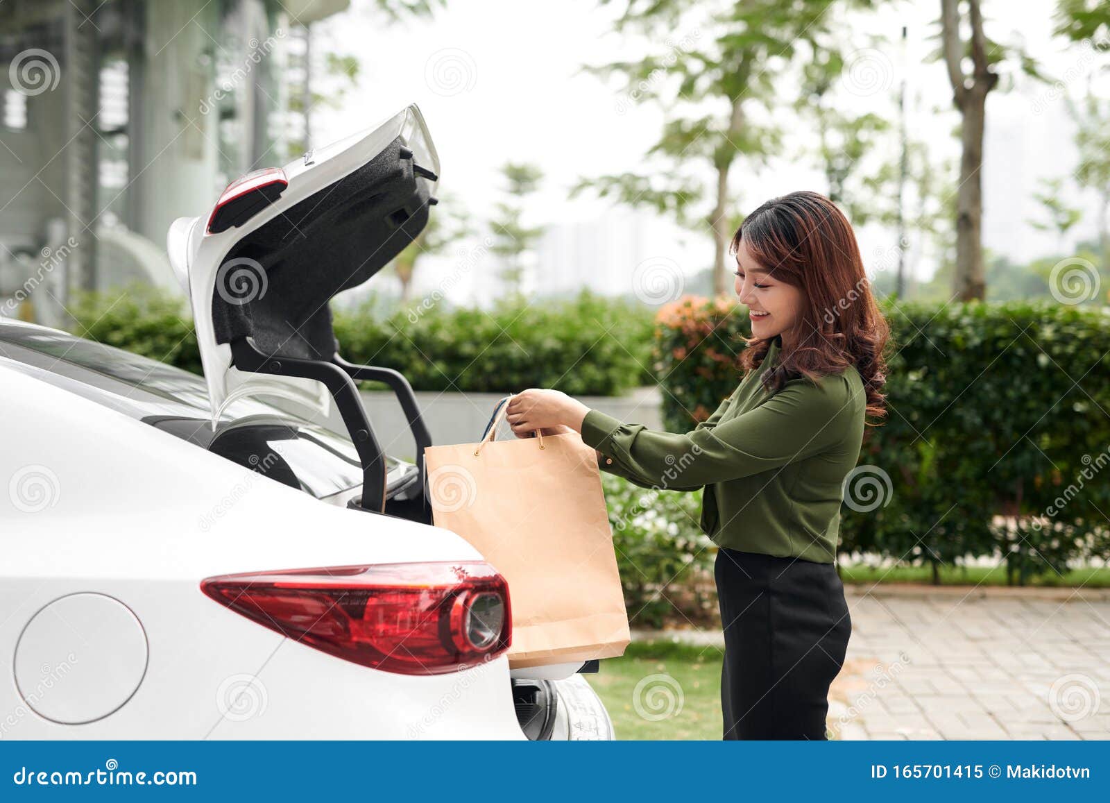 Smiling Asian Woman Putting Her Shopping Bags Into The Car Trunk Stock