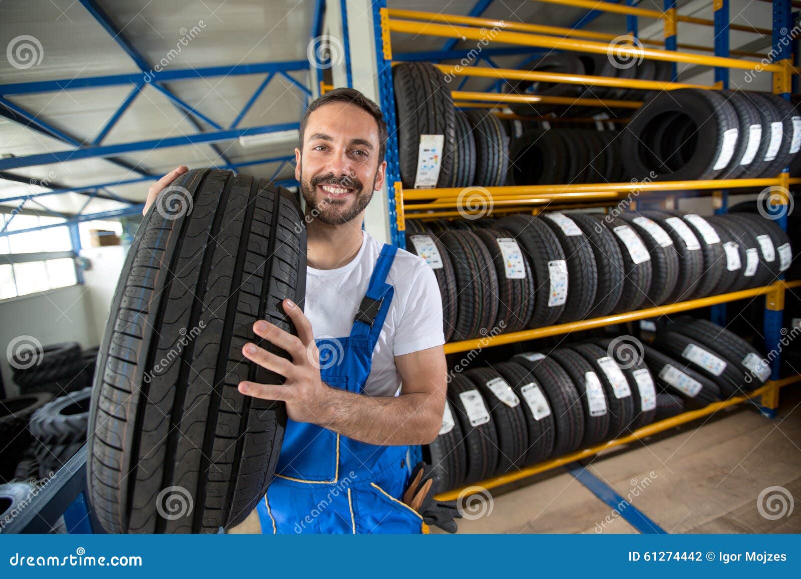 Smiling Auto Mechanic Carrying Tire Stock Photo - Image of blue, sale ...
