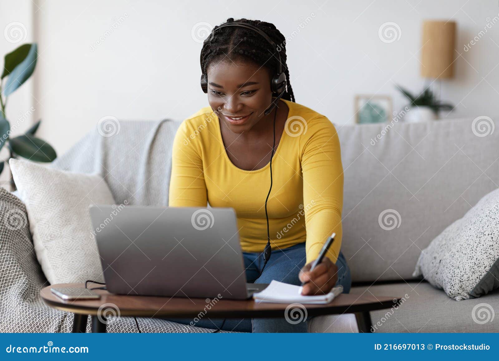 Smiling Black Lady In Headset Writing Notes While Watching Webinar On ...