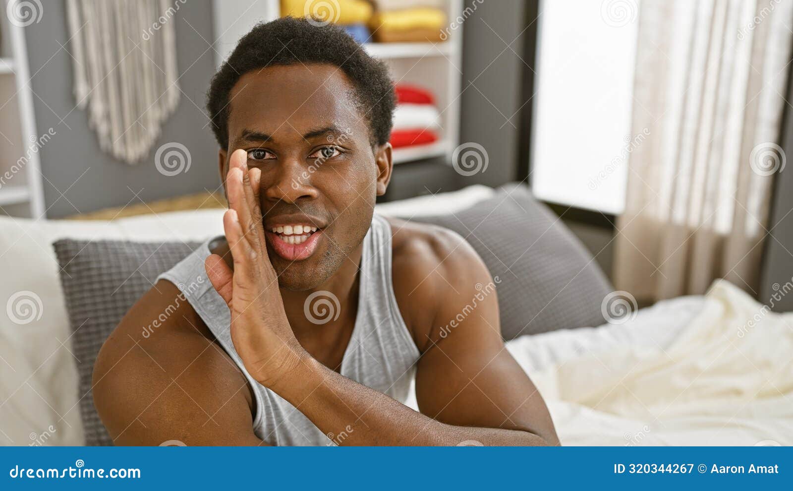 A Smiling Black Man Makes a Secret-telling Gesture in a Cozy Bedroom ...