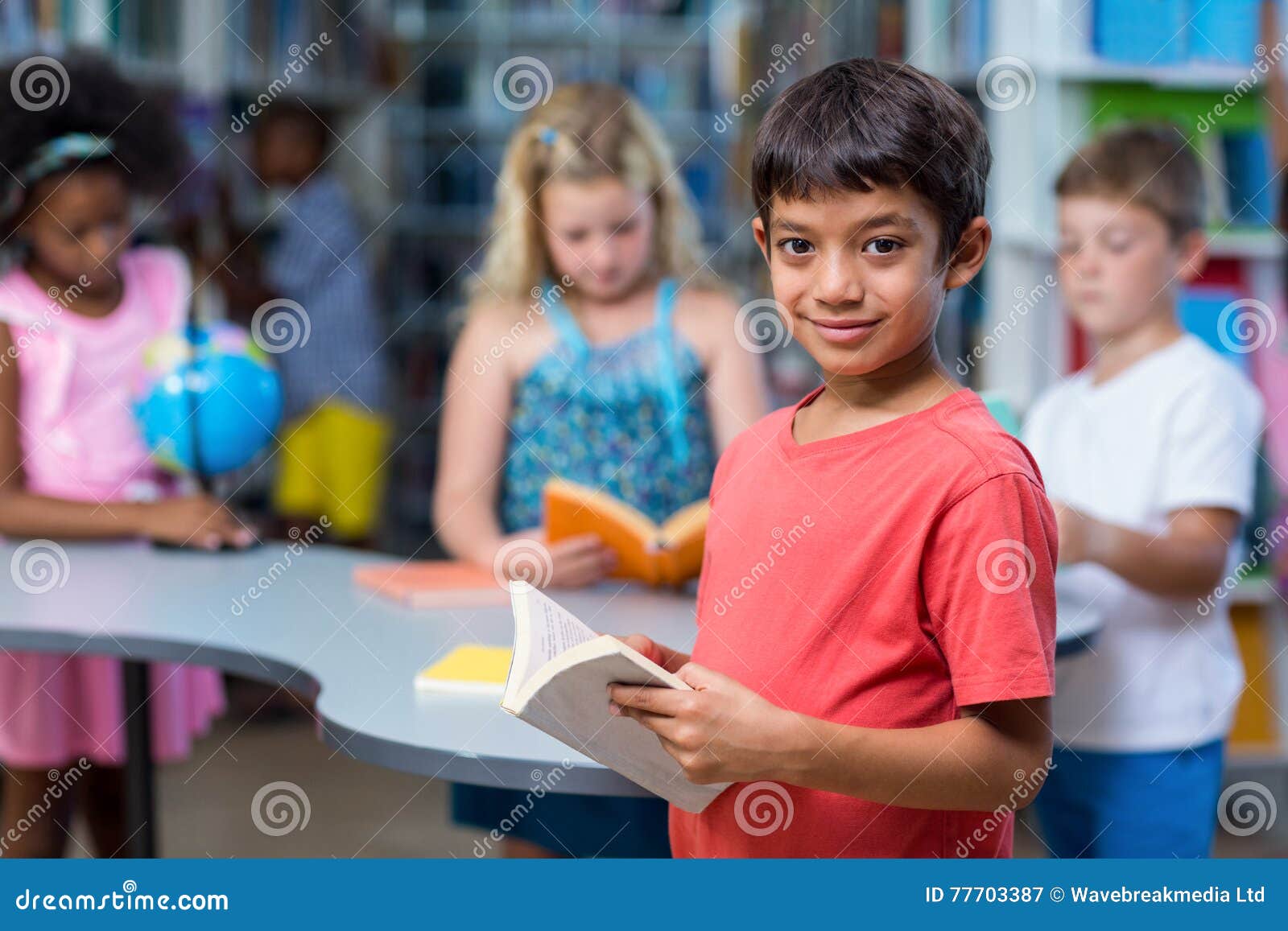 Smiling Boy Holding Books Against Classmates Stock Image - Image of ...