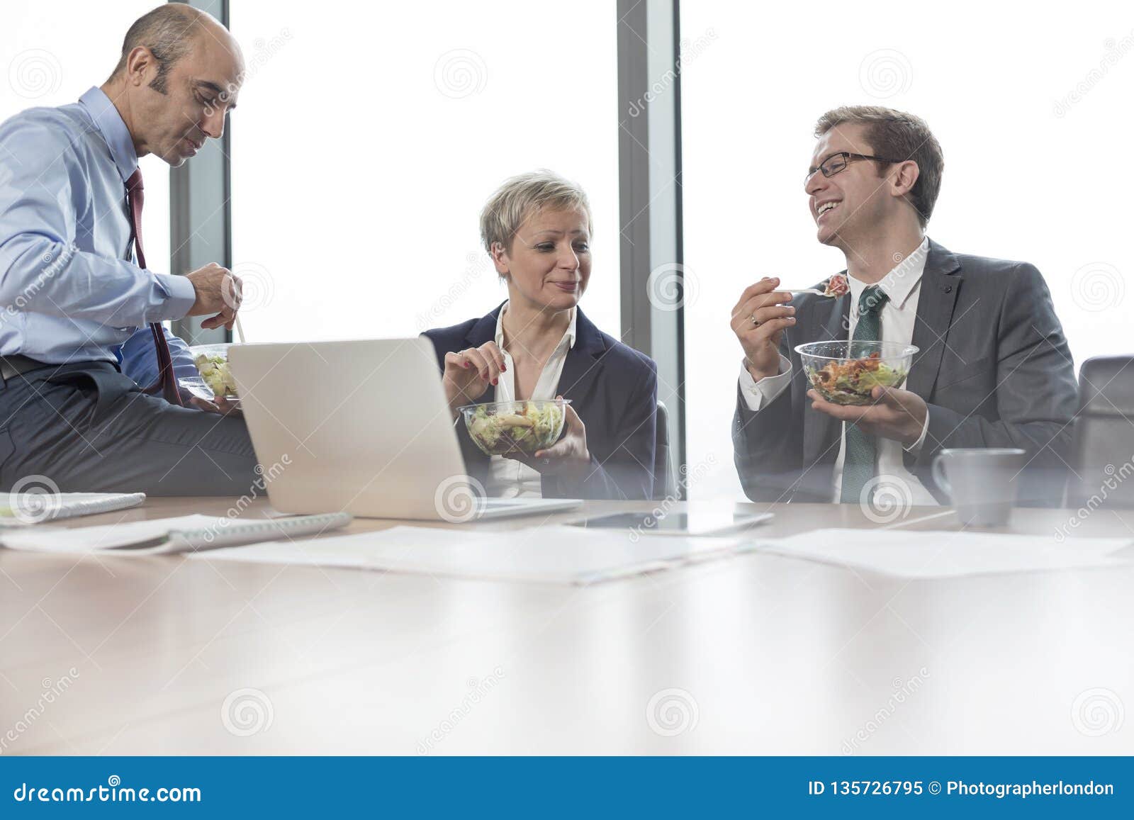 Smiling Business Colleagues Eating Lunch while Sitting in Boardroom ... Smiling Business Colleagues Eating Lunch while Sitting in Boardroom ...