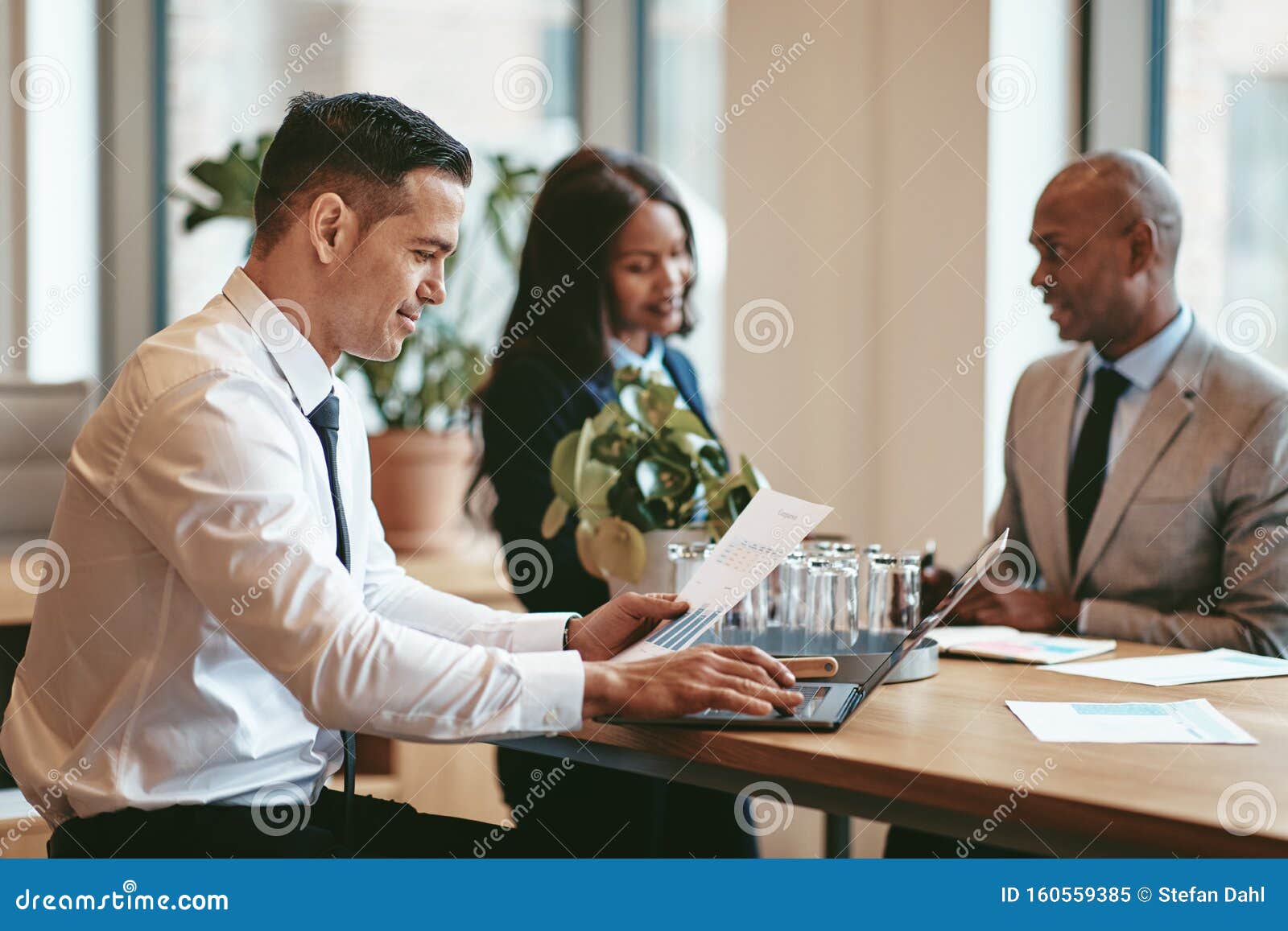 Smiling Businessman Reading Paperwork and Using a Laptop at Work Stock ...