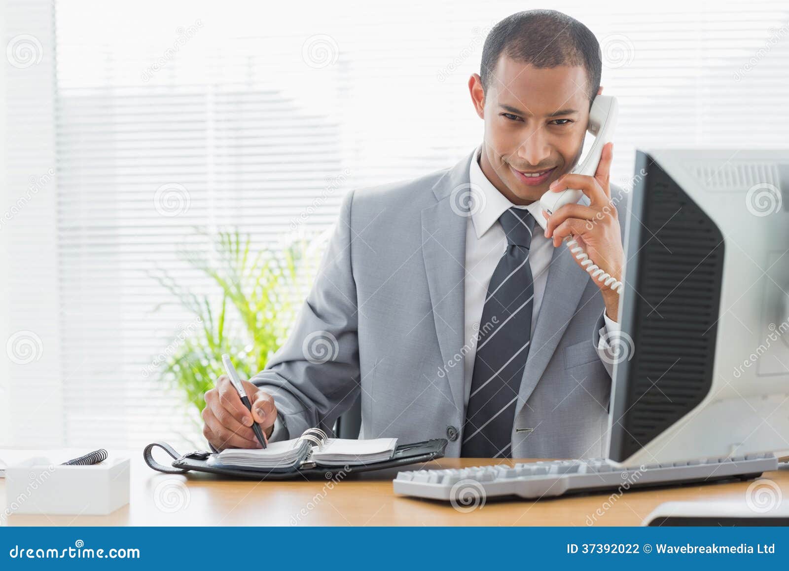 Smiling Businessman Using Computer and Phone at Office Stock Photo ...