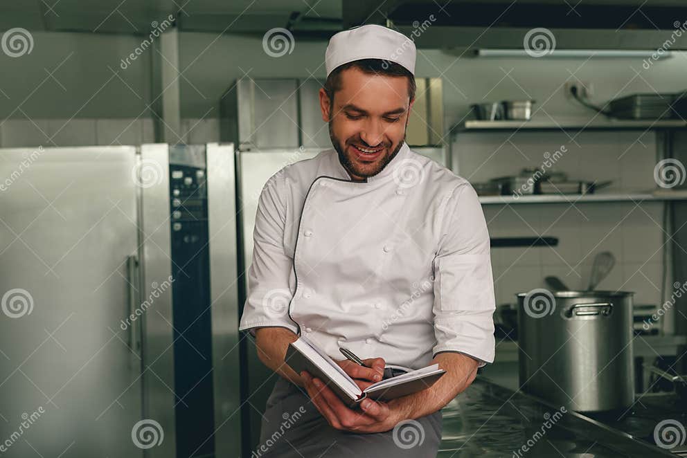 Smiling Chef in Uniform Making Notes in Notebook Standing on Kitchen ...