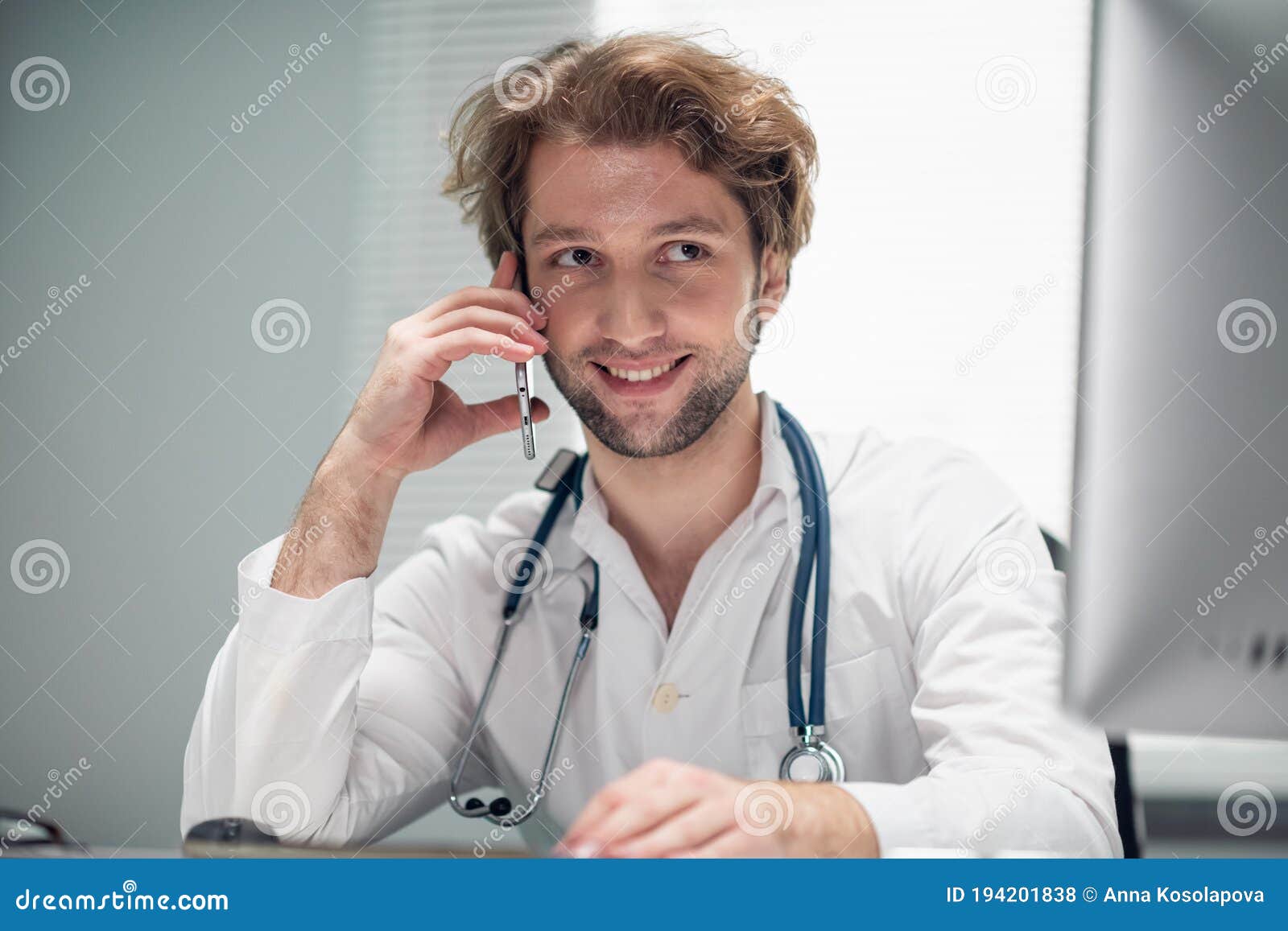 A Smiling Doctor Talking on the Phone, while Looking at the Computer ...