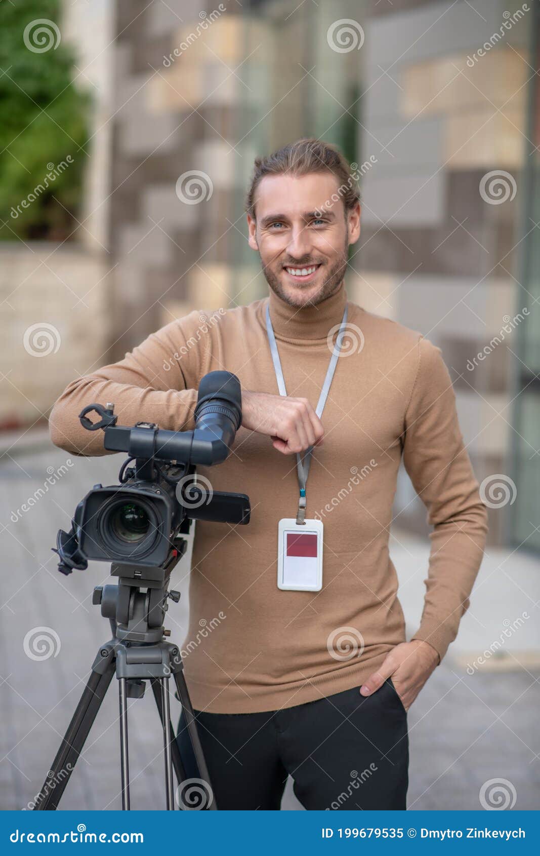 Smiling Fair-haired Cameraman Standing Next To Camera, Leaning on Elbow ...