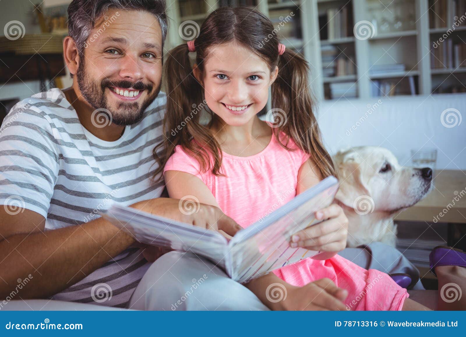 Smiling Father And Daughter Looking At Photo Album In Living Room Stock
