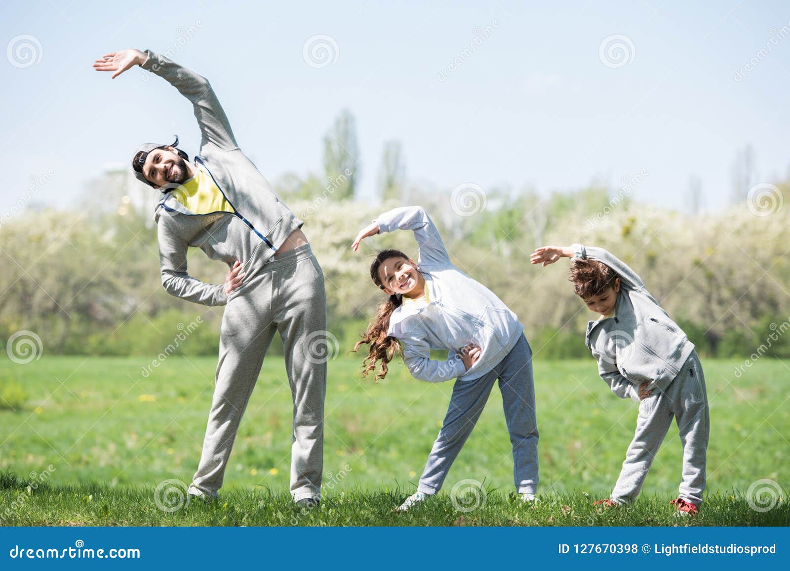 Smiling Father with Daughter and Son Doing Physical Exercise on Grassy ...