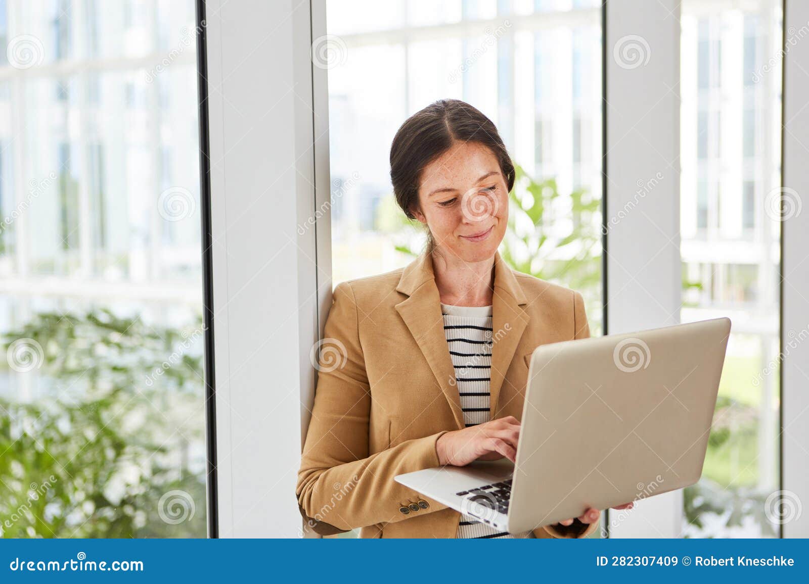 Smiling Female Entrepreneur Using Laptop while Leaning on Window in ...