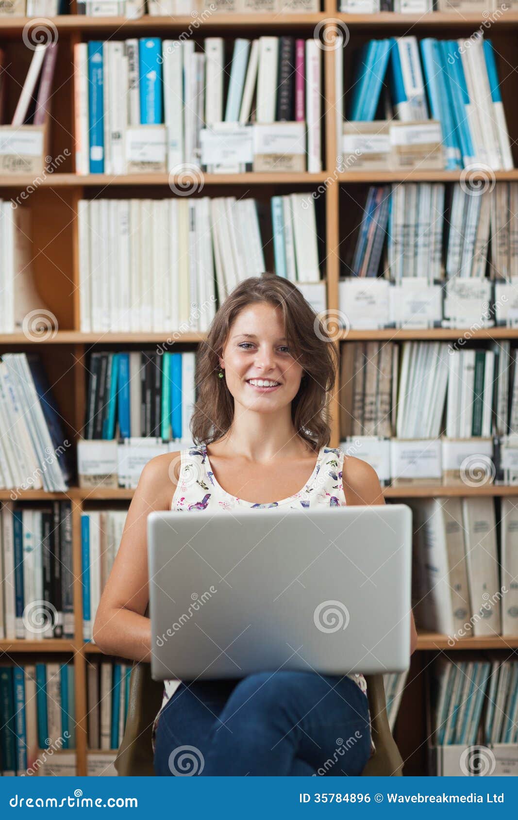 Smiling Female Student Against Bookshelf Using Laptop in Library Stock ...