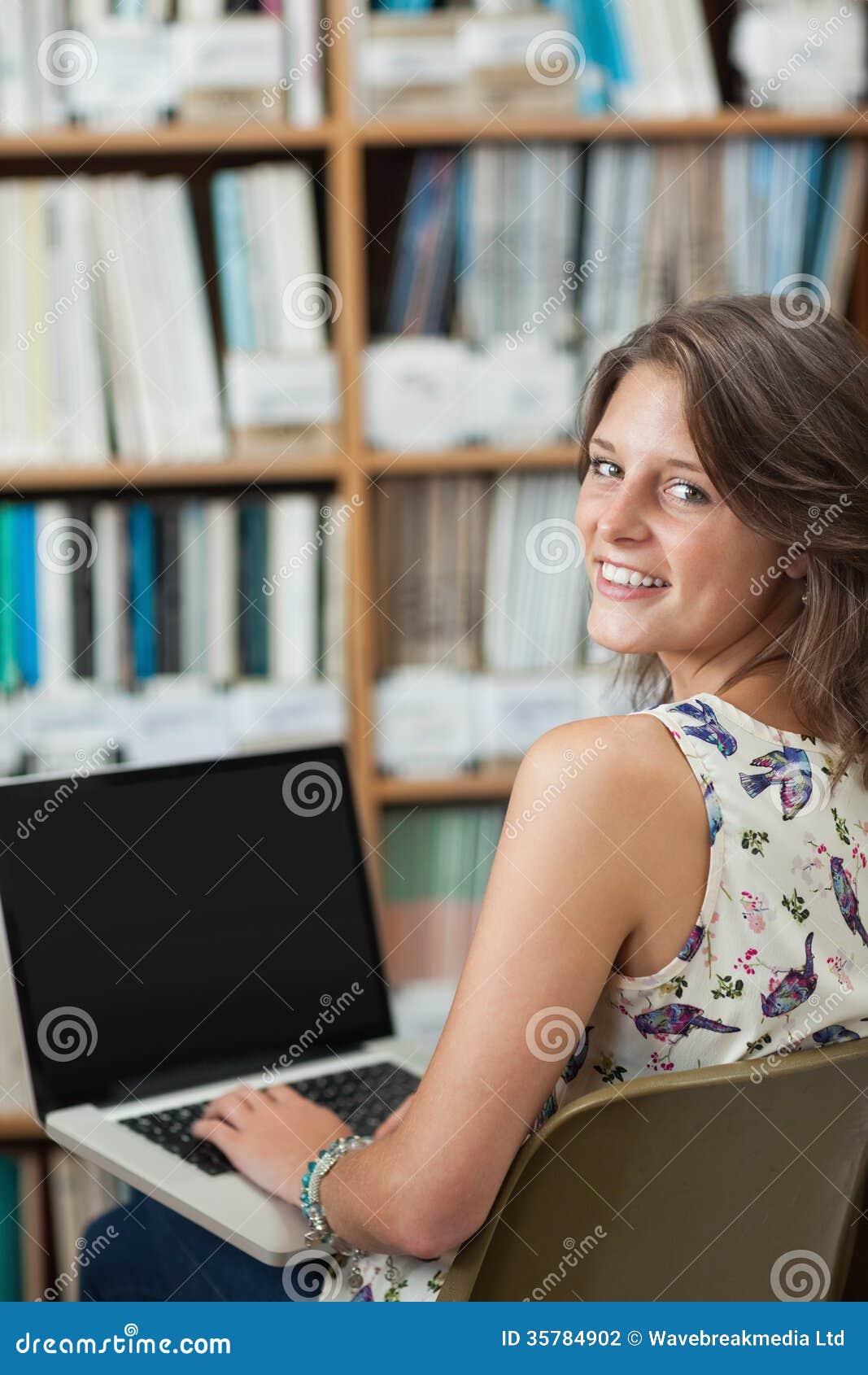Smiling Female Student Against Bookshelf Using Laptop in Library Stock ...
