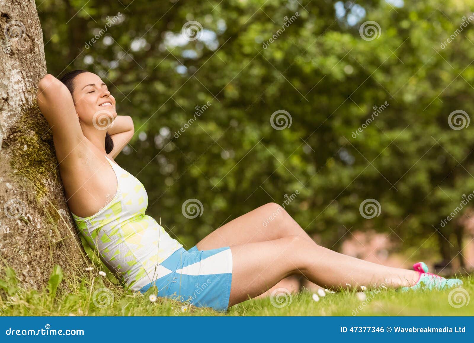 Smiling Fit Brunette Sitting and Relaxing Against a Tree Stock Photo ...