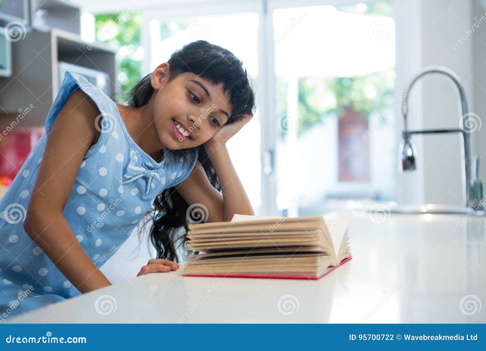 Smiling Girl Reading Novel at Kitchen Counter Stock Photo - Image of ...
