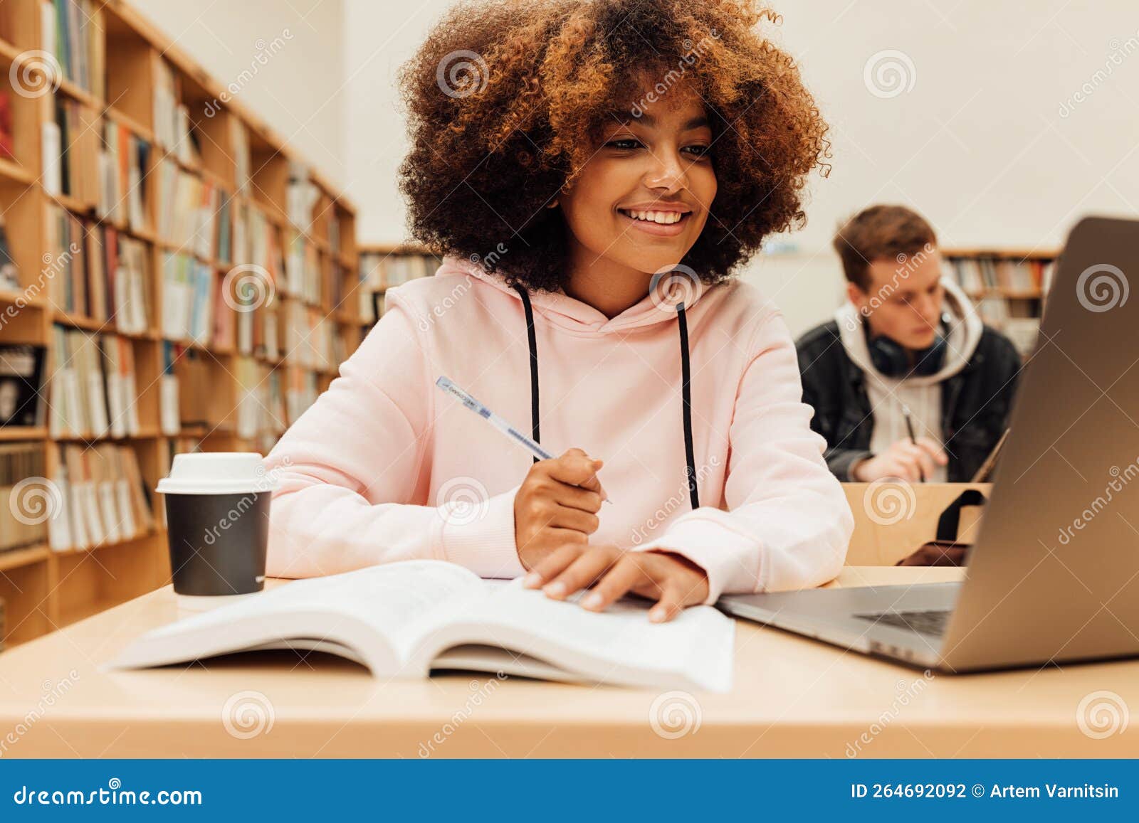 Smiling Girl Sitting at a Table in the Library and Looking at a Laptop ...