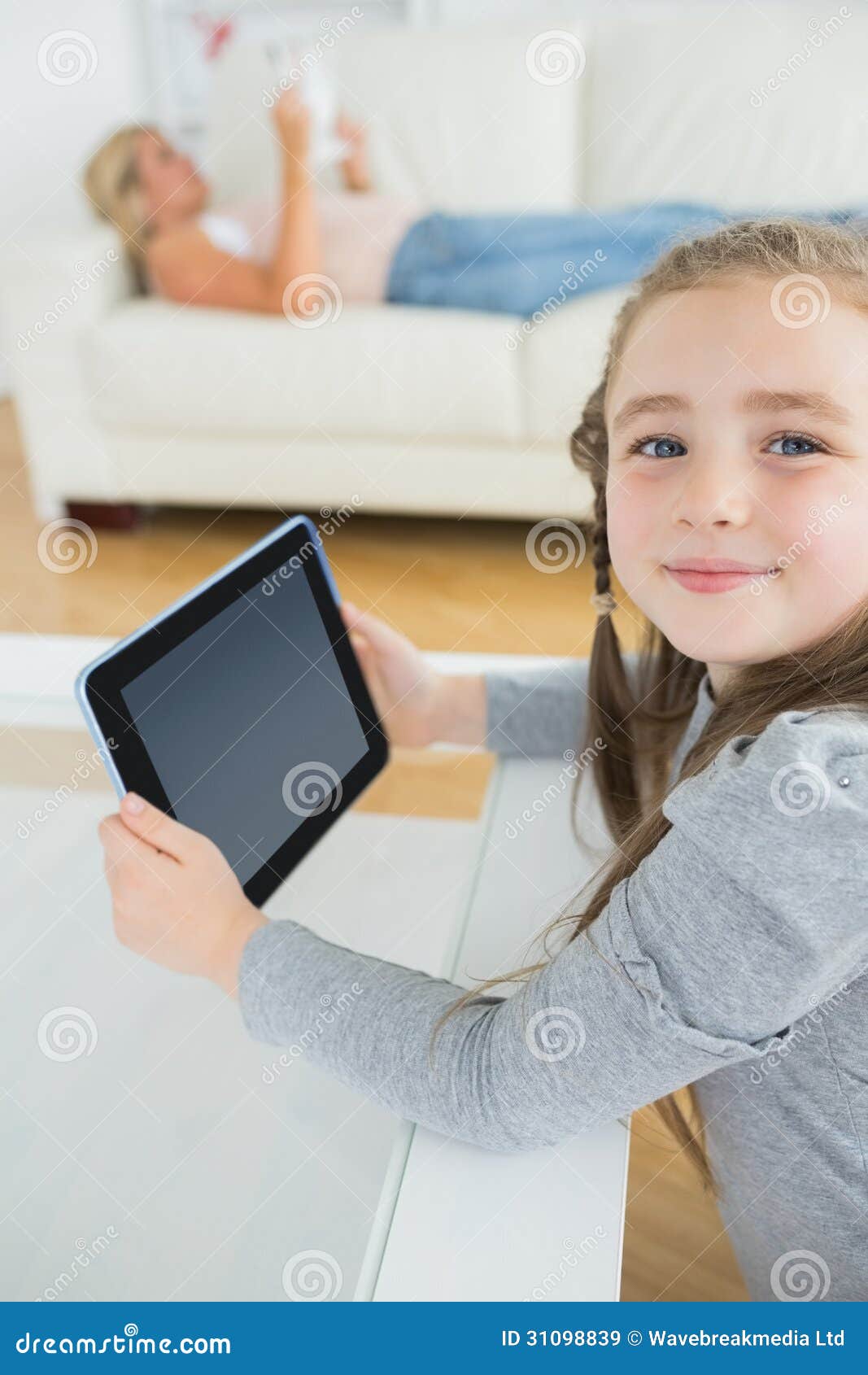 Smiling Girl Using Tablet Computer while Mother is Reading Newspaper ...