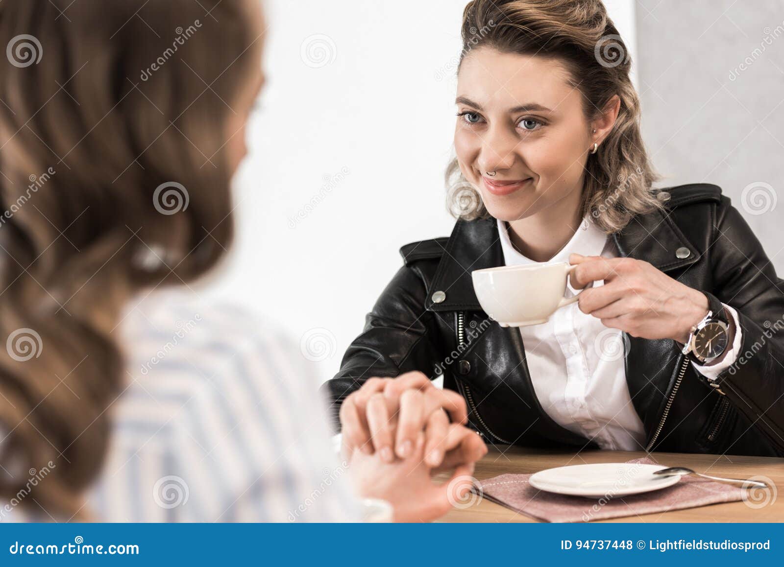 Smiling Girlfriends Sitting at Cafe and Holding Hands while Drinking ...