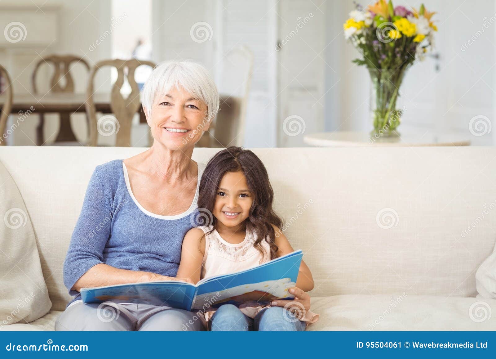 Smiling Grandmother And Granddaughter Sitting Together On Sofa With