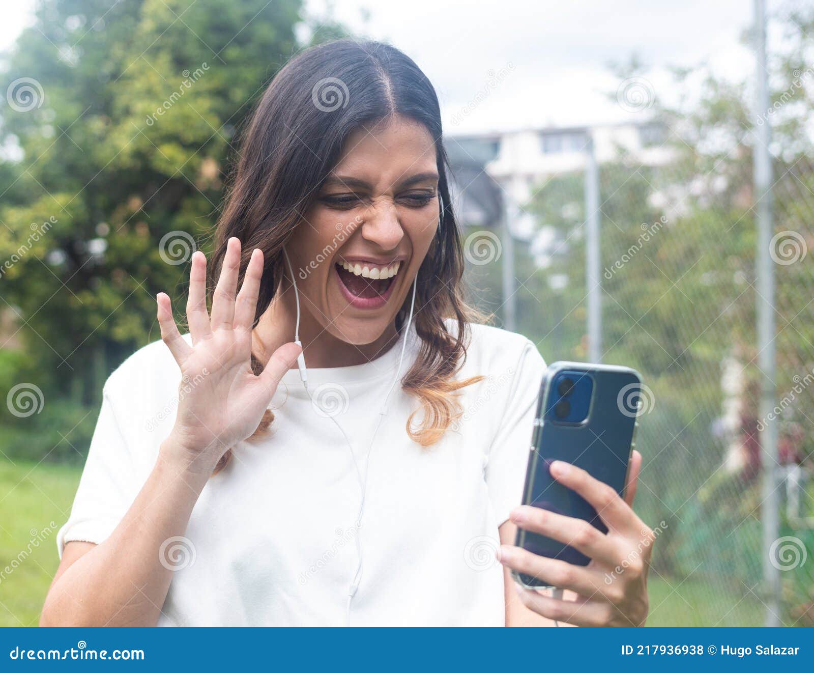 Smiling Latina Woman Waving At Cell Phone Camera In Video Call Stock