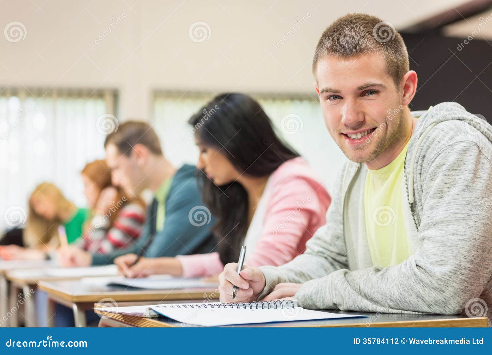Smiling Male Student with Others Writing Notes in Classroom Stock Photo ...