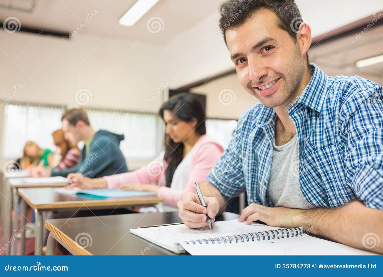 Smiling Male Student with Others Writing Notes in Classroom Stock Photo ...