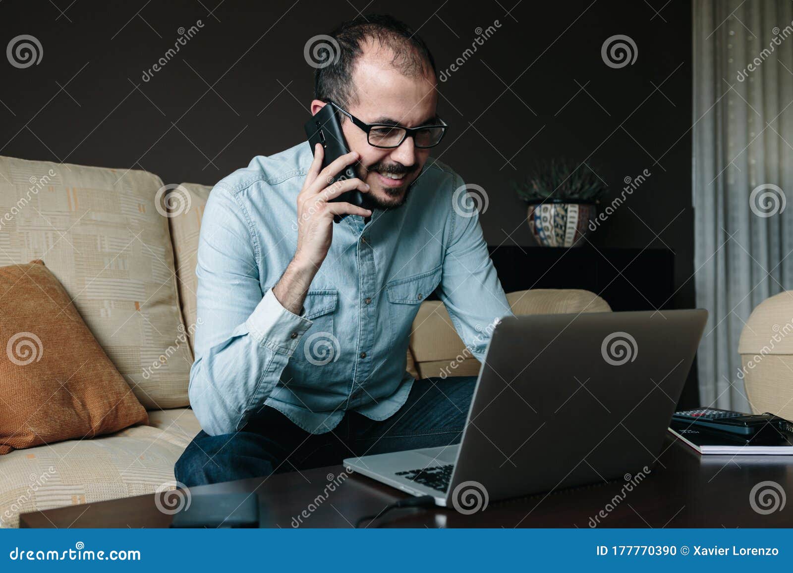 Smiling Man Calling from Home while is Reading the News on the Laptop ...