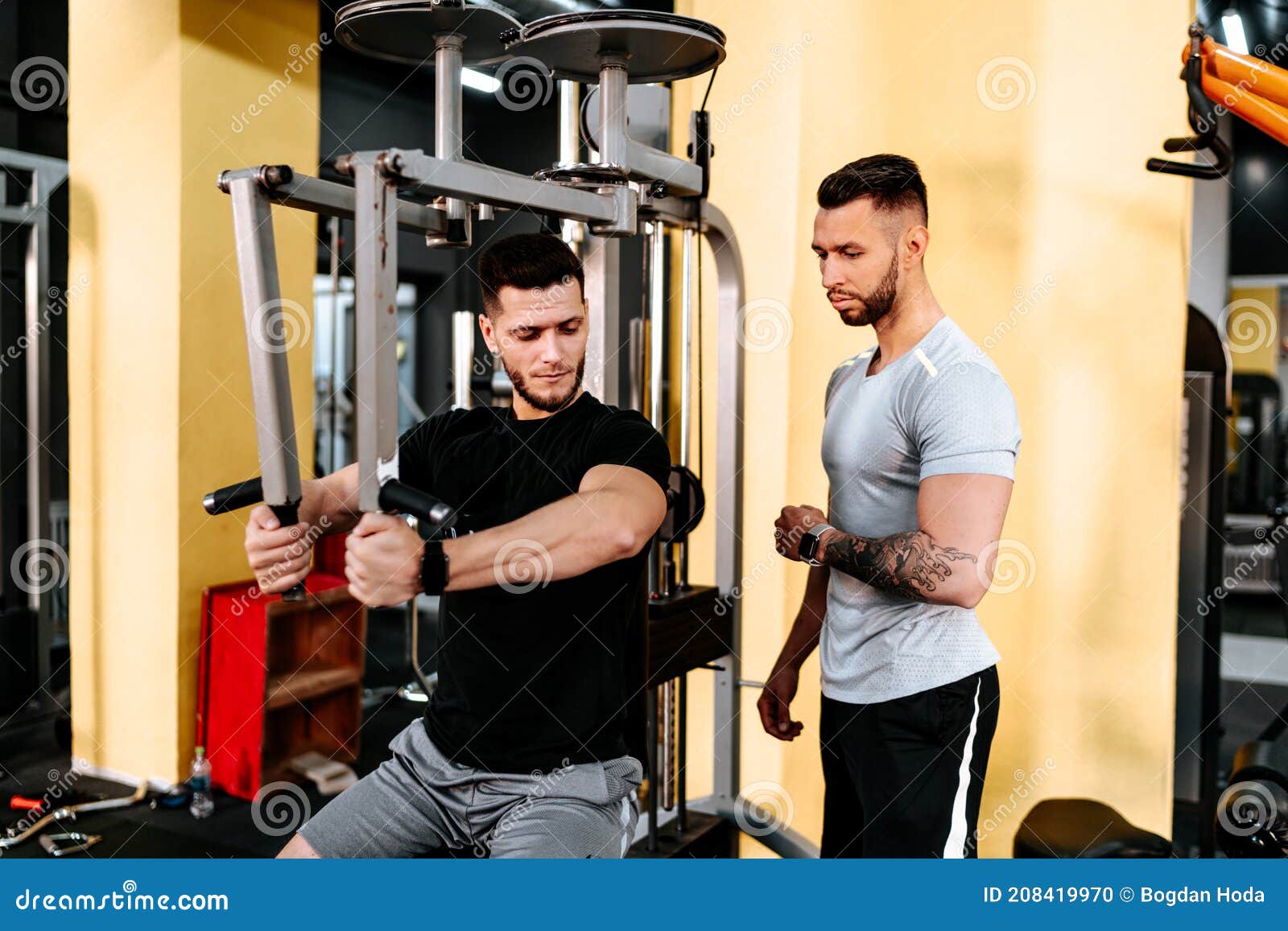 Smiling Man Learning at the Gym, Doing Chest Exercises with Assistance ...