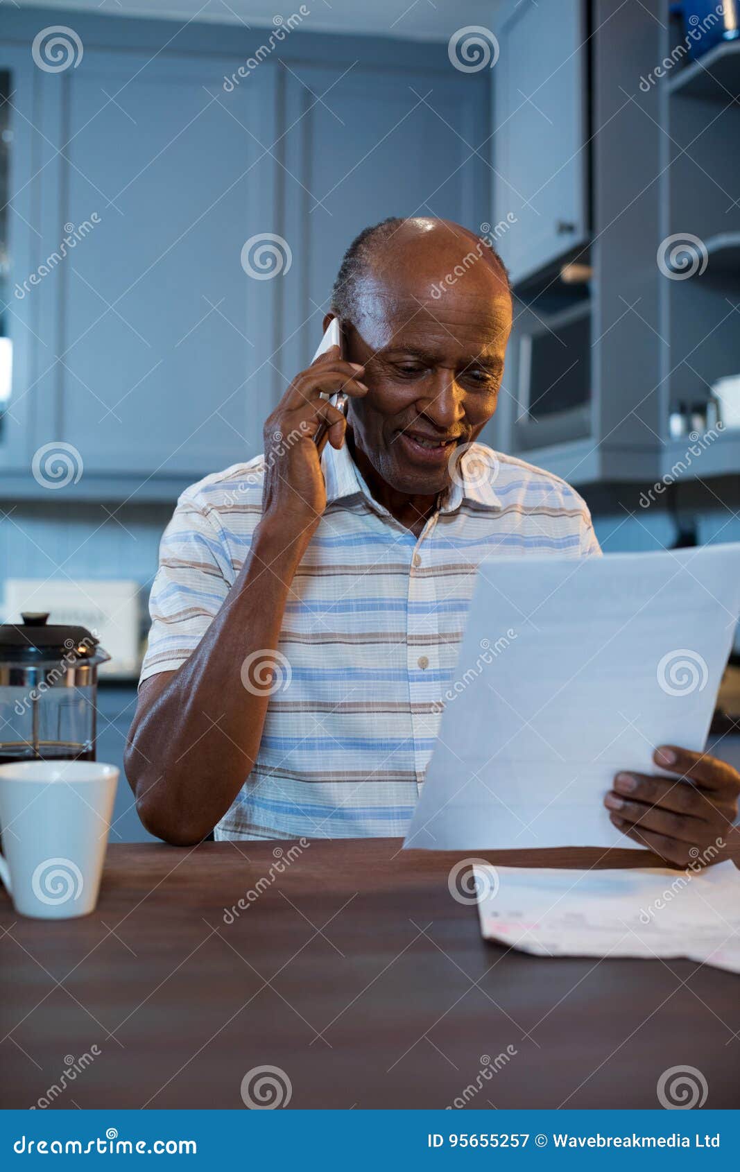 Smiling Man Reading Document while Using Phone at Home Stock Image ...