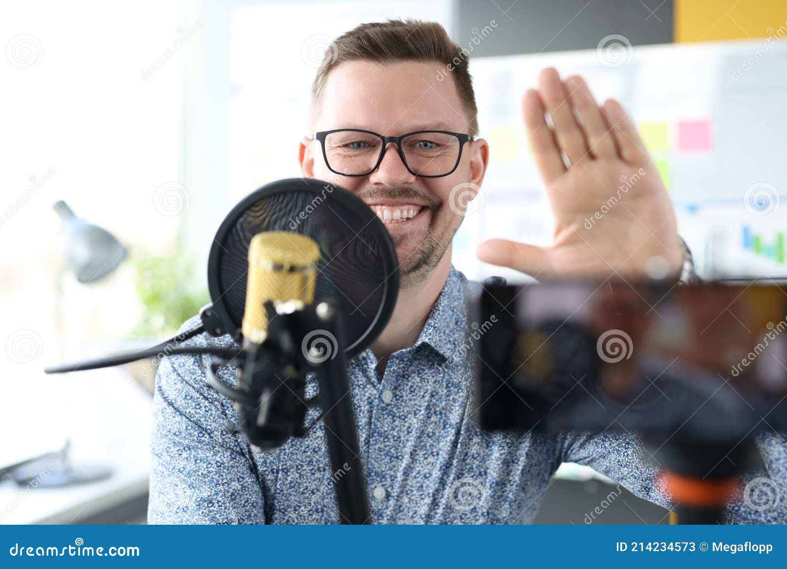 Smiling Man Sits in Front of a Microphone and Waves at Camera with His ...