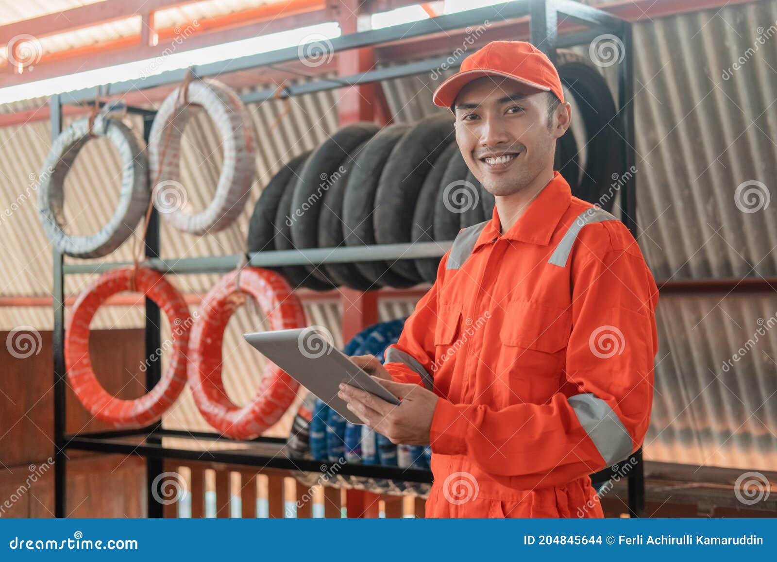 Mechanic In Wearpack Uniform With A Thumbs Up While Picking Up A Tire ...