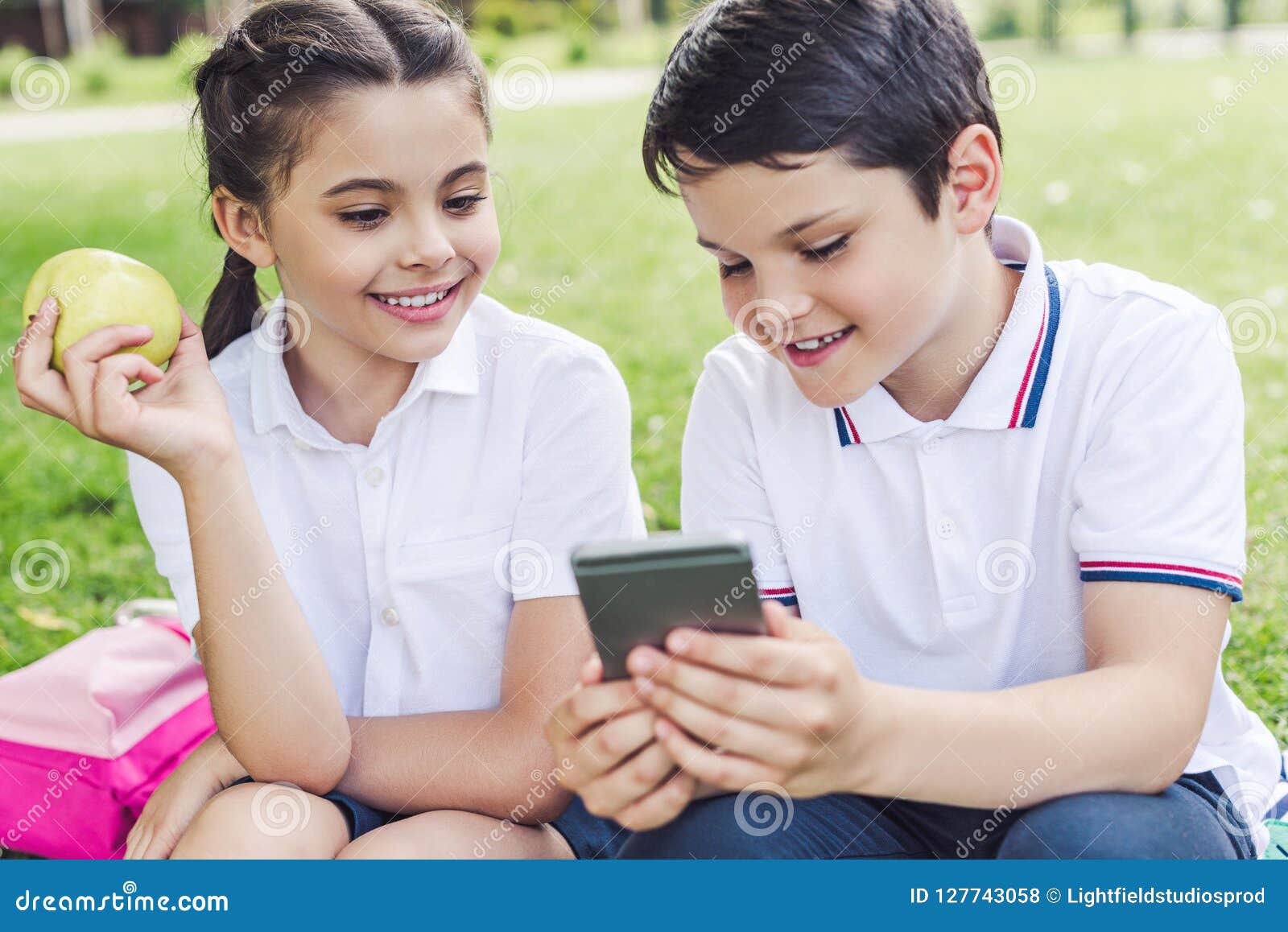 Smiling Schoolchildren Using Smartphone Together while Sitting Stock ...