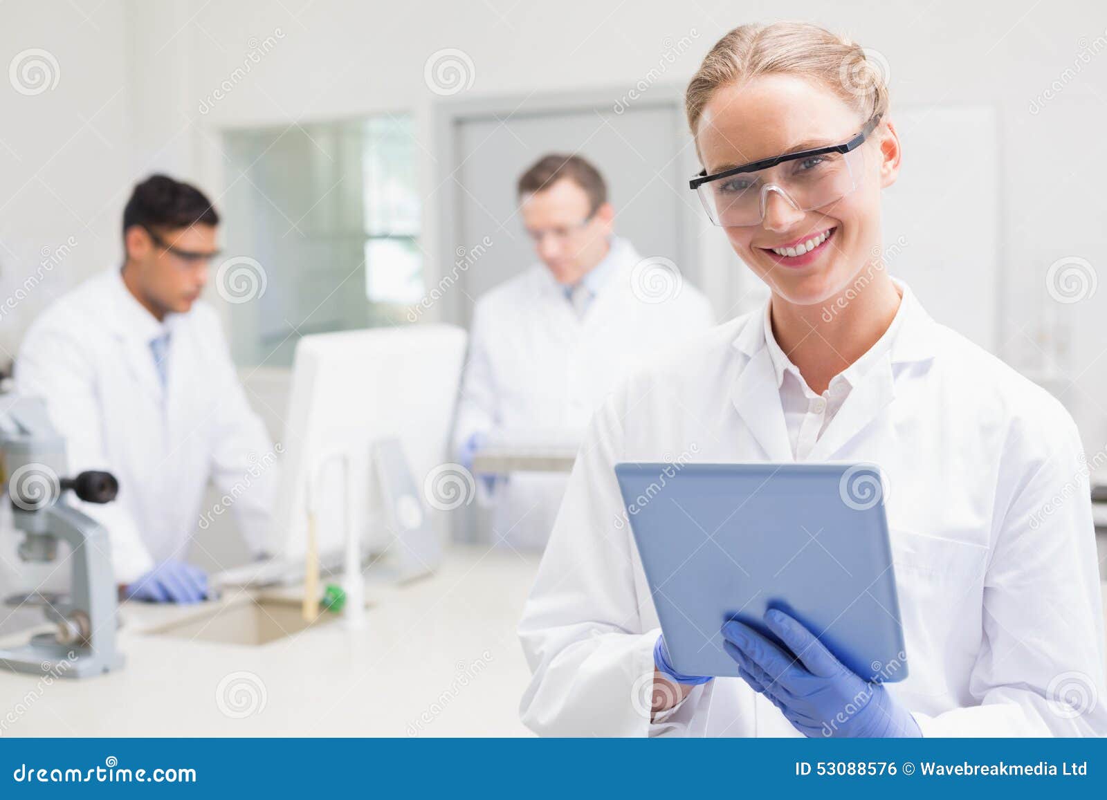 Smiling Scientist Using Tablet while Colleagues Working Behind Stock ...
