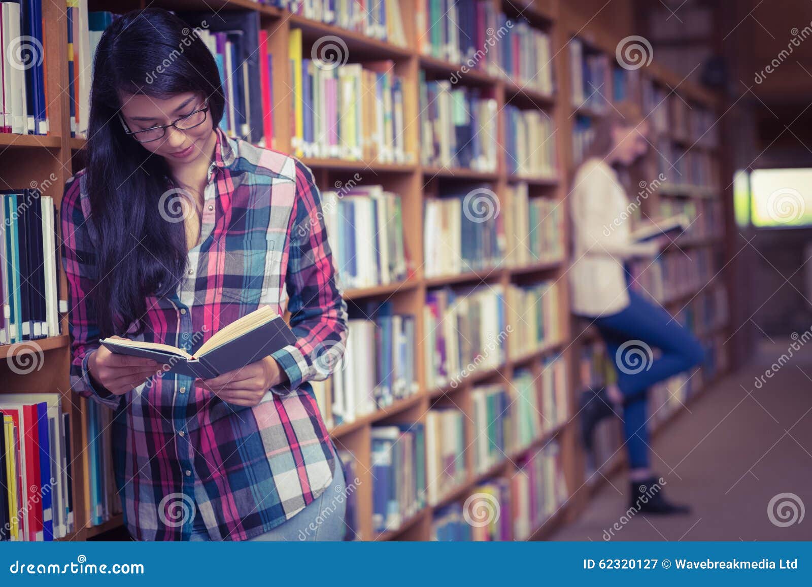 Smiling Student Leaning Against Bookshelves Reading Book Stock Image ...