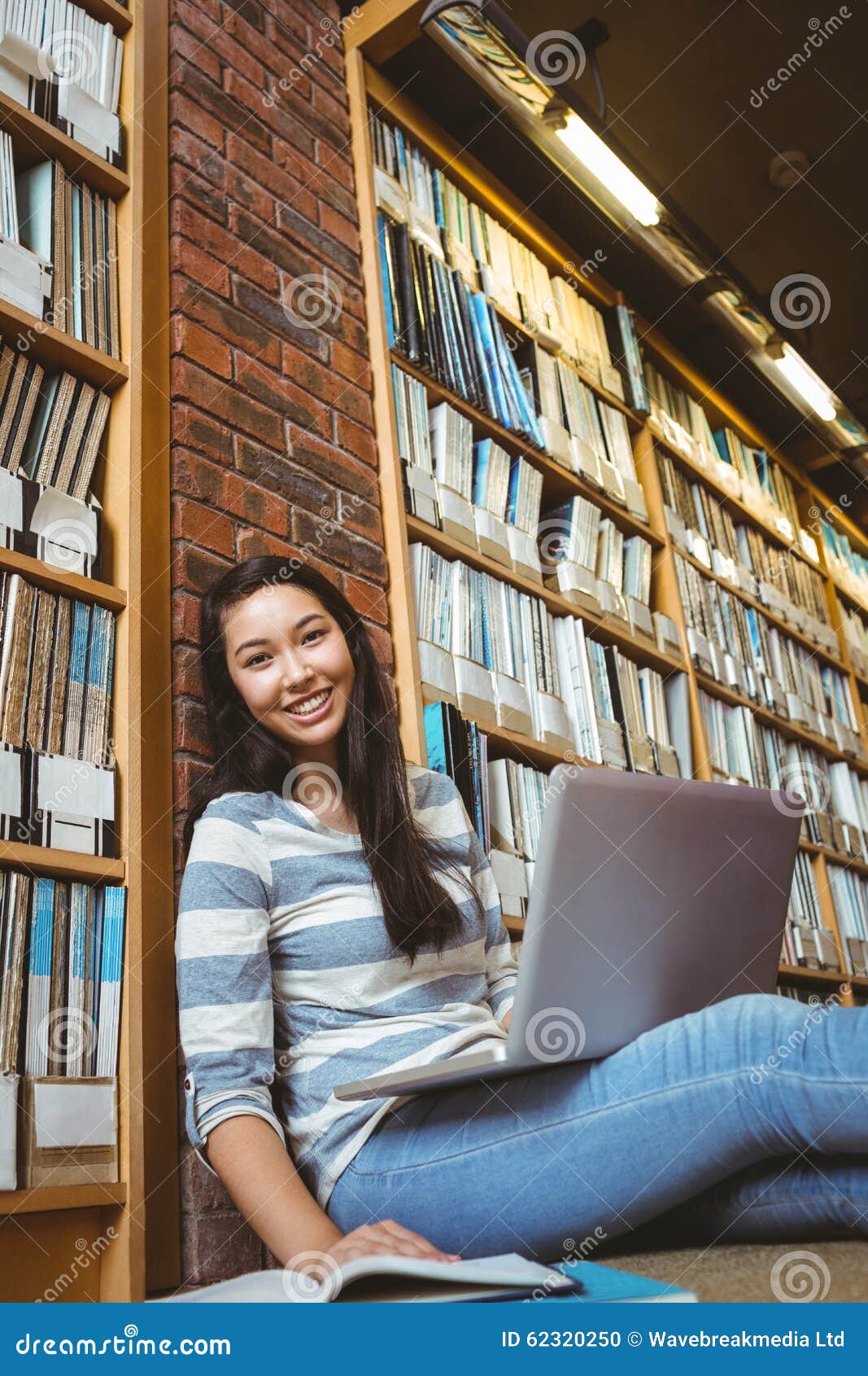Smiling Student Sitting on the Floor Against Wall in Library Studying ...