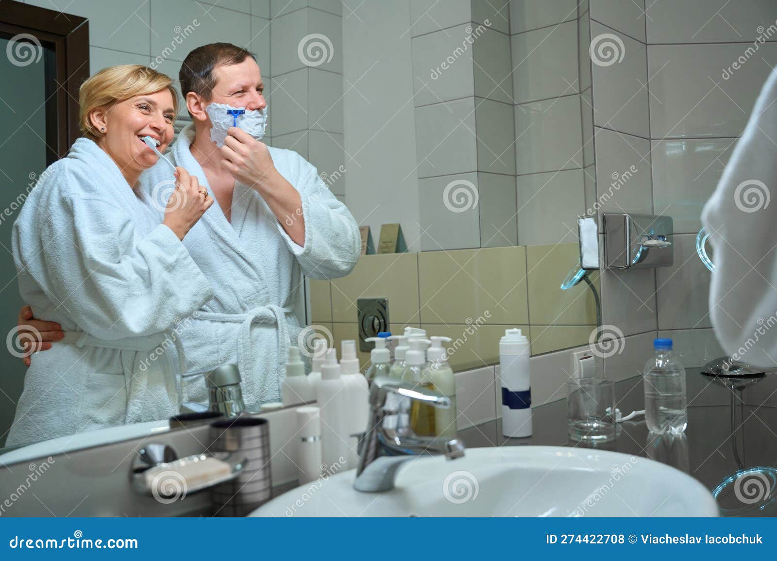 Smiling Woman Brushing Her Teeth While Man Shaves In Bathroom Stock
