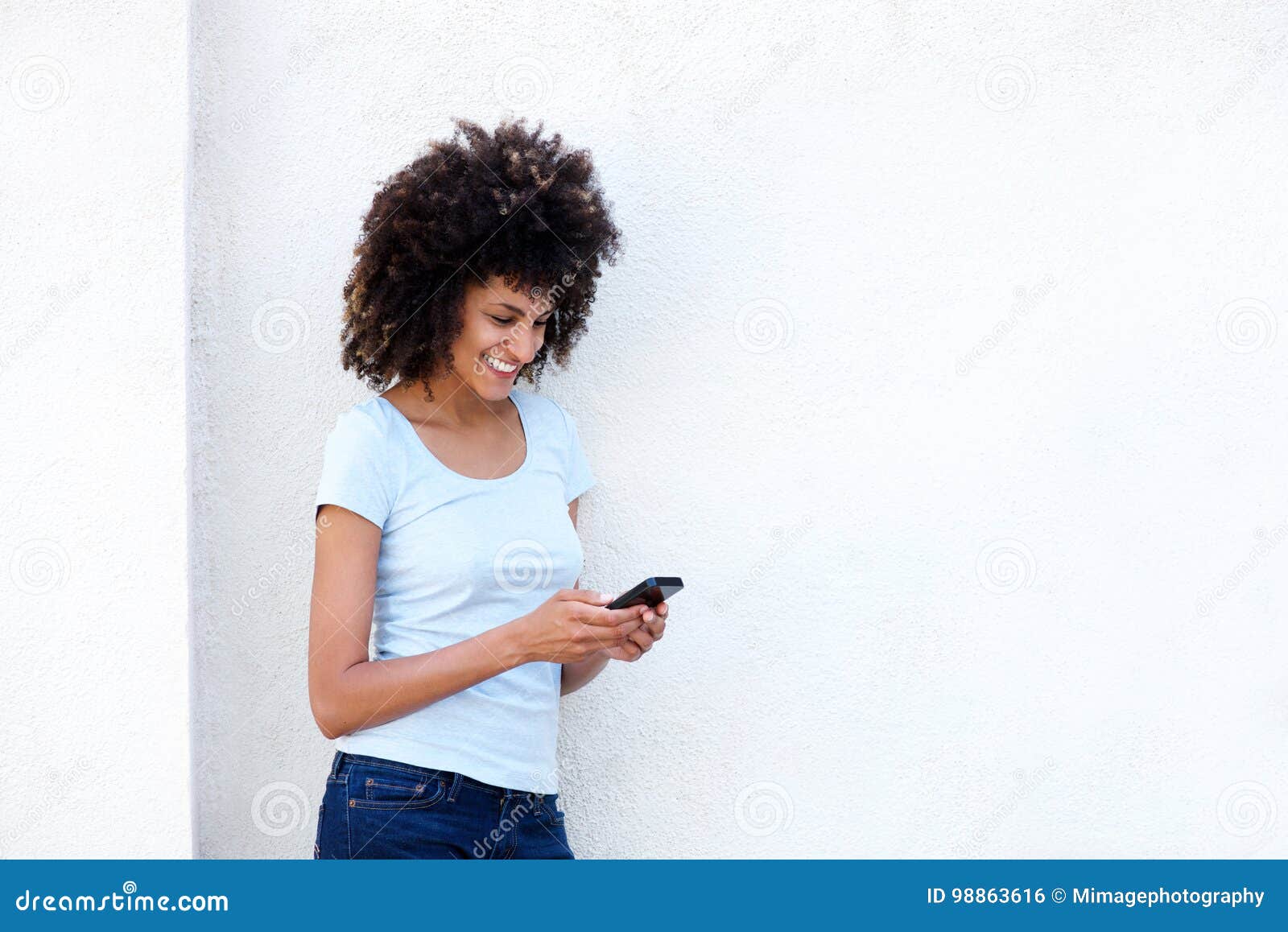 Smiling Woman Holding Cellphone Standing by White Wall Stock Photo ... Smiling Woman Holding Cellphone Standing by White Wall Stock Photo ...