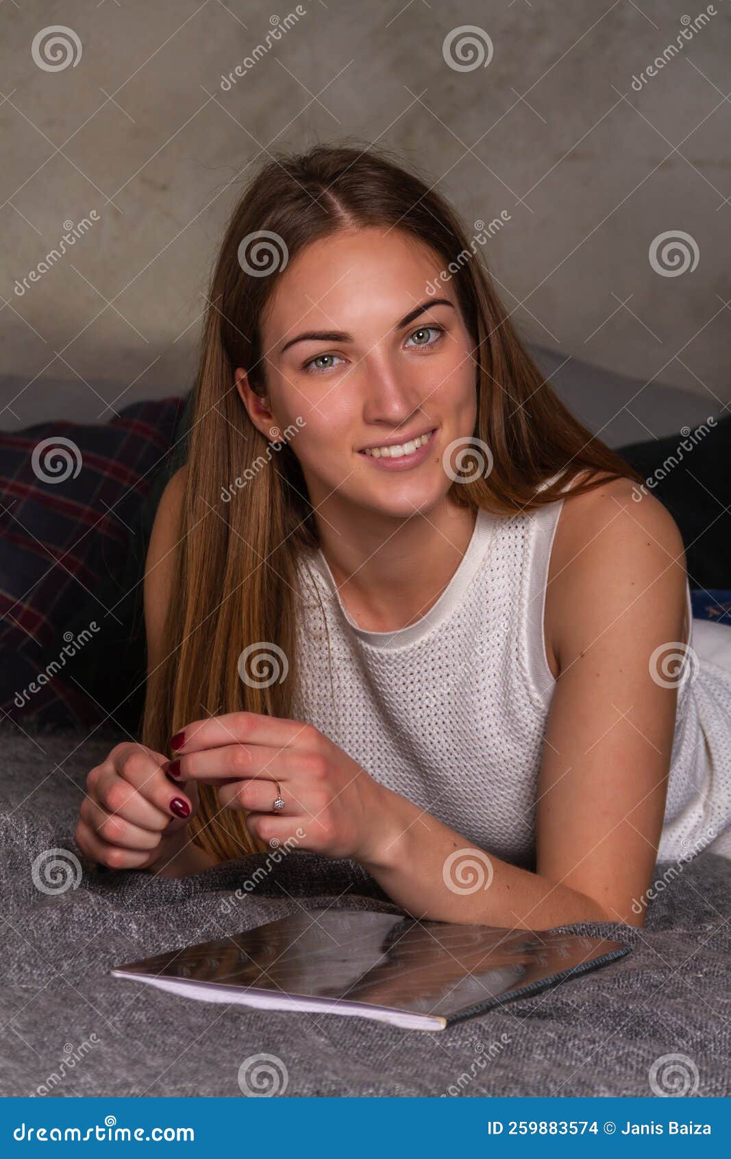 Smiling Woman Lying On Her Stomach In Bed With A Notebook And Playing