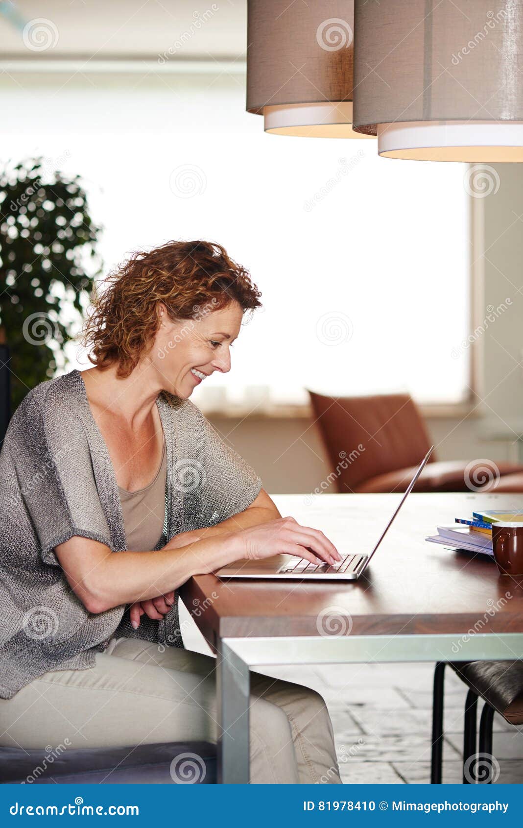 Smiling Woman Sitting at Table Working on Laptop Stock Photo - Image of ...