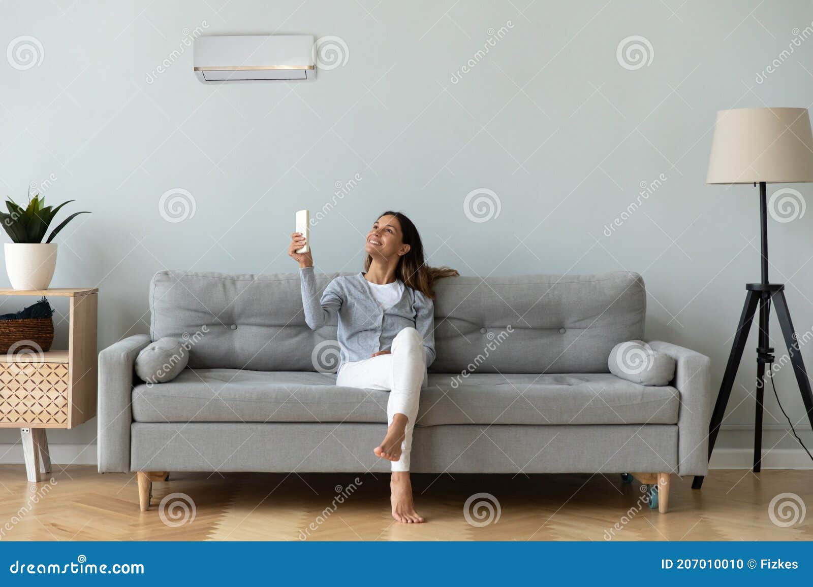 Smiling Woman Using Air Conditioner Remote Controller, Sitting on Couch ...