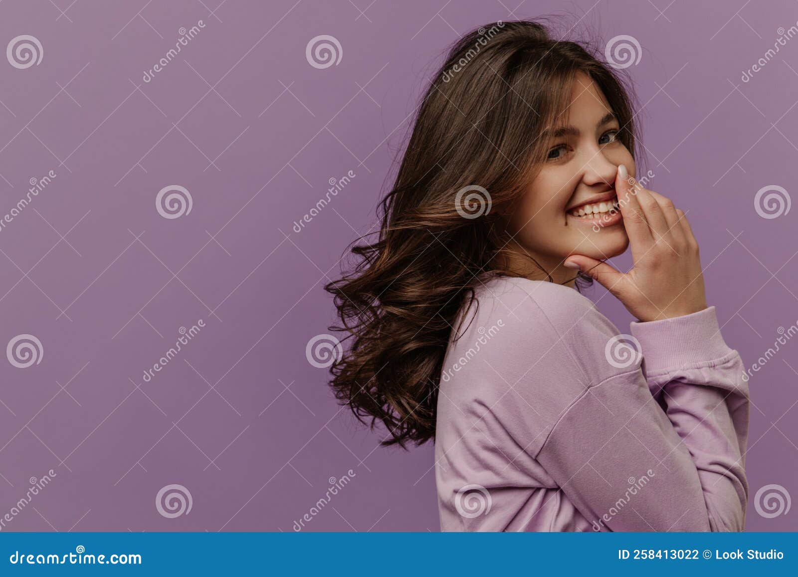 Smiling Young Caucasian Girl Looks Into Camera With Her Hand Near Face