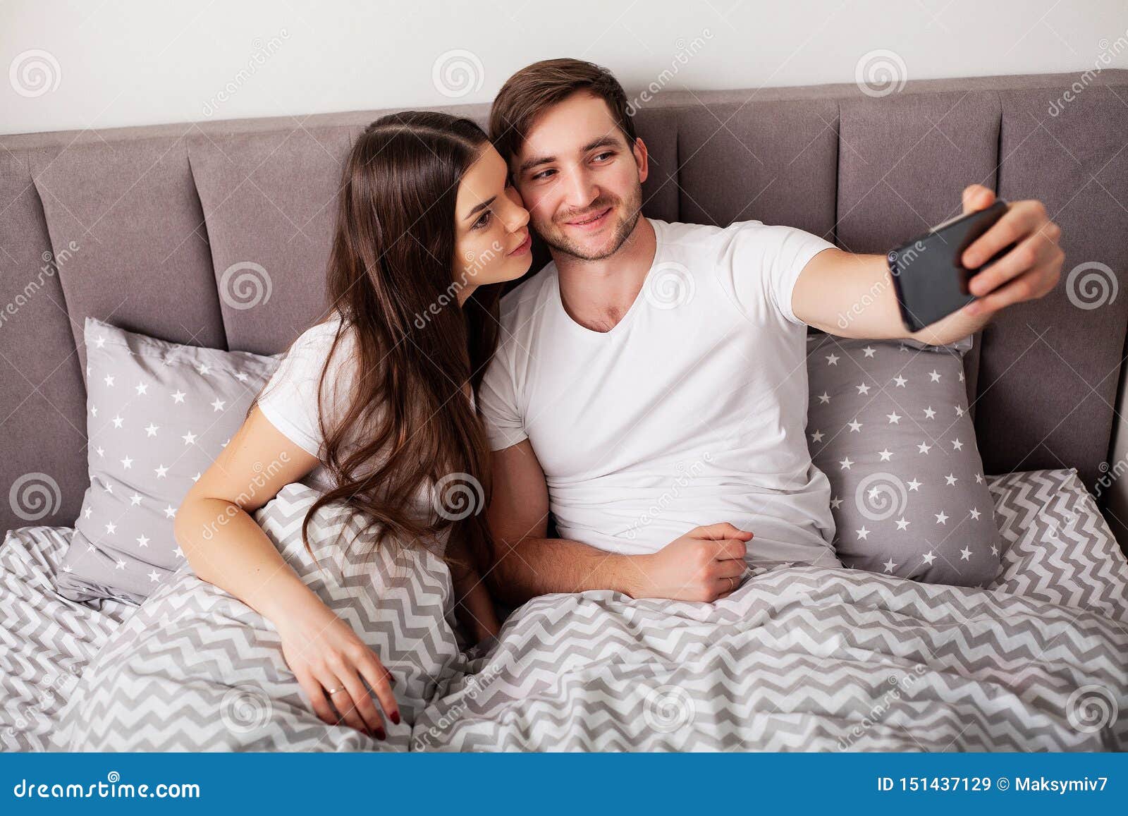 Smiling Young Couple Taking Selfie Together In Bedroom Stock Image