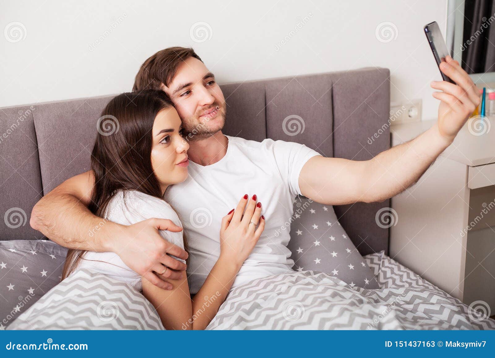 Smiling Young Couple Taking Selfie Together In Bedroom Stock Image