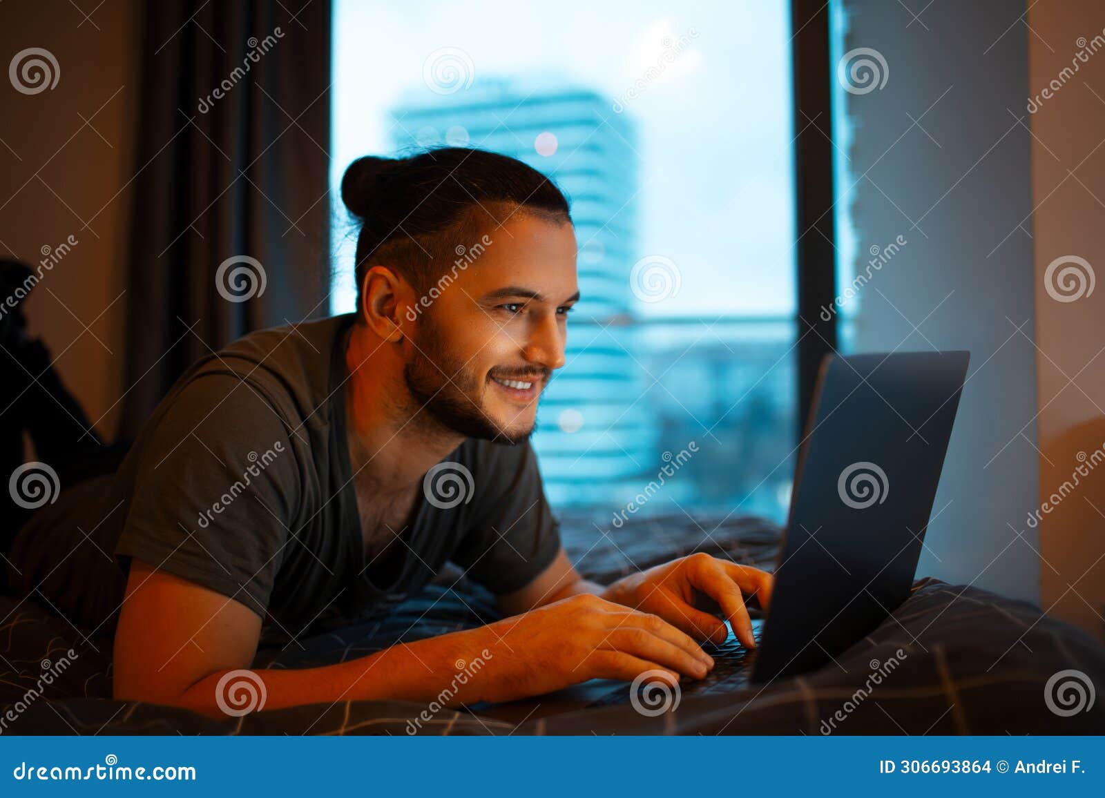 Smiling Young Guy Lying on Bed and Working Home on Laptop. Typing on ...