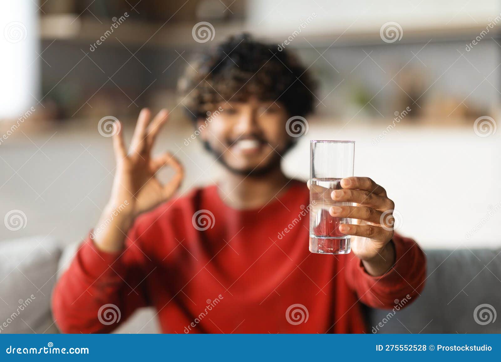 Smiling Young Indian Guy Holding Glass Of Water And Showing Ok Gesture
