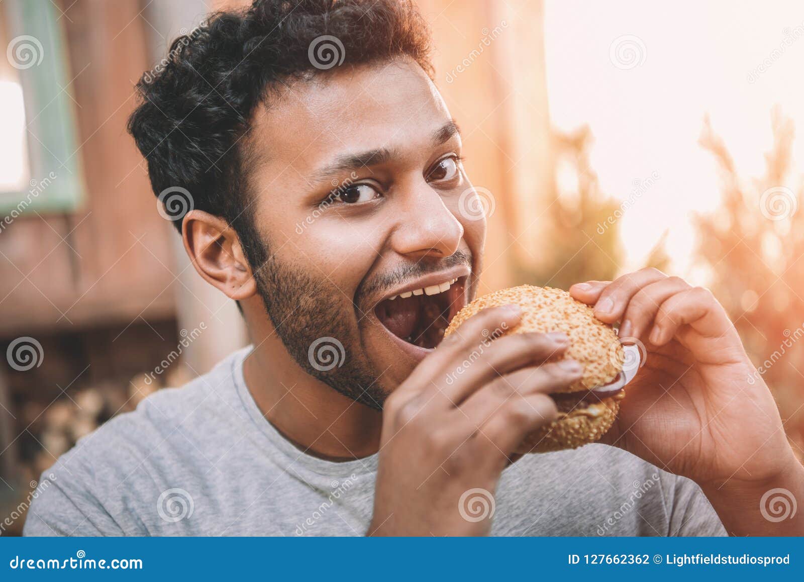 Smiling Young Man Biting Fresh Hamburger and Looking Stock Photo ...