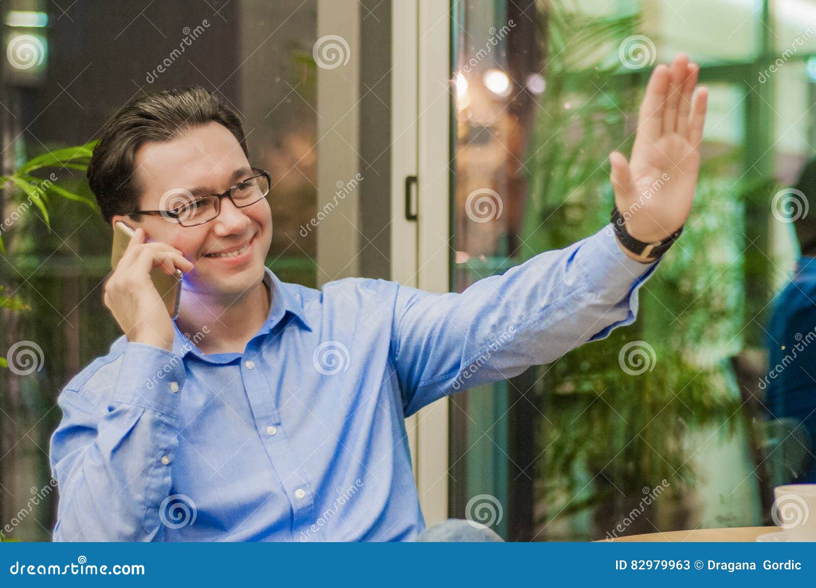 Smiling Young Man Talking on the Phone and Showing Greeting Gesture ...