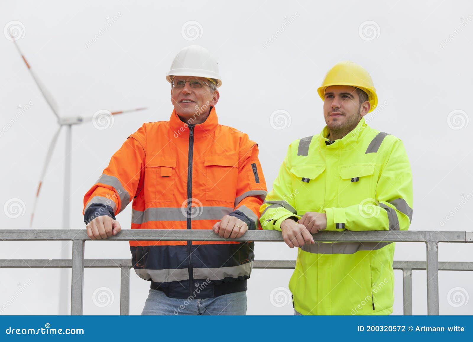 Smiling Young and Mature Engineers in Front of Blurred Wind Turbine ...