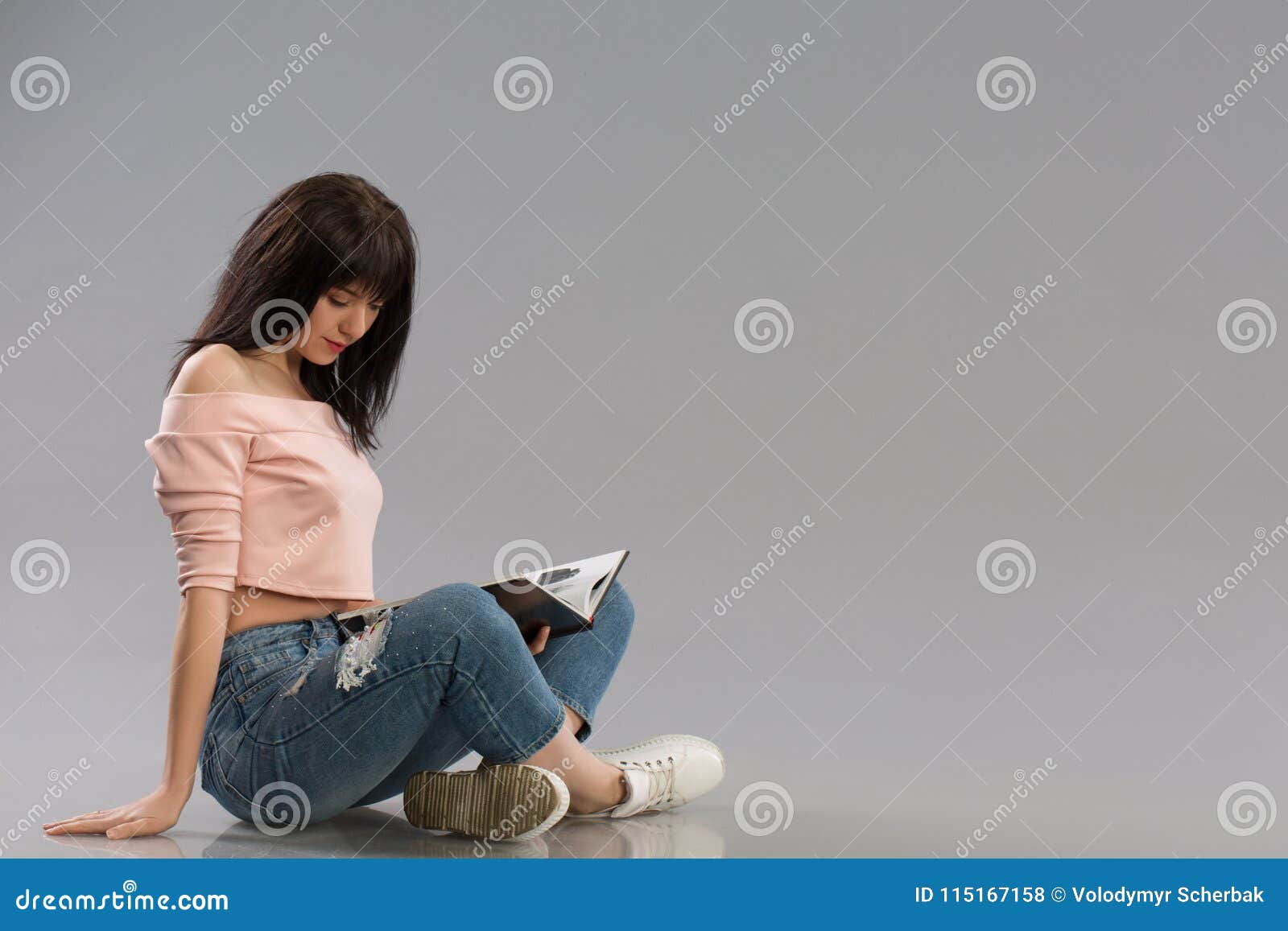 Smiling Young Woman Reading A Book Sitting On Grey Background Stock
